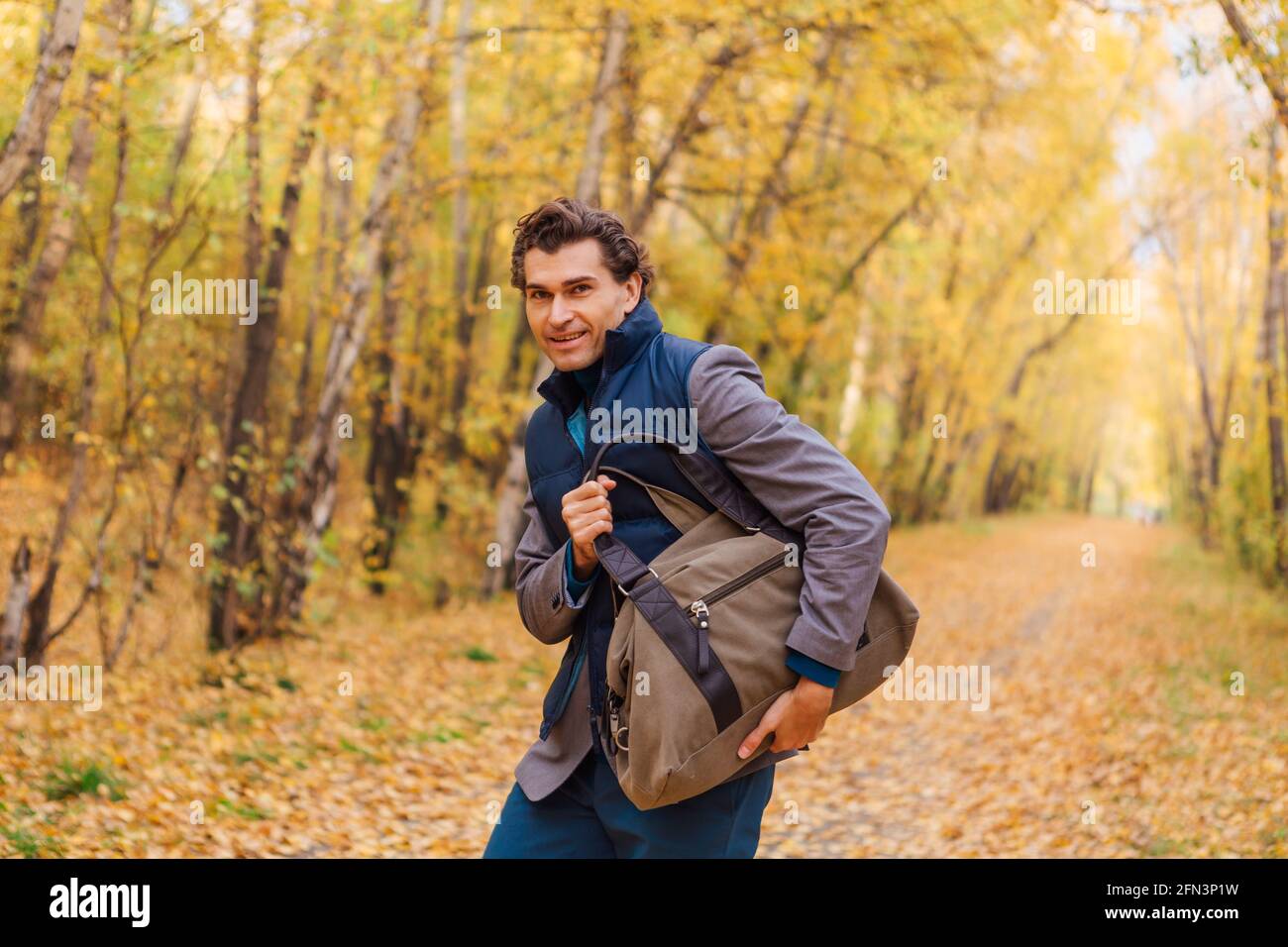 Tall handsome man with a bag in the autumn alley Stock Photo - Alamy