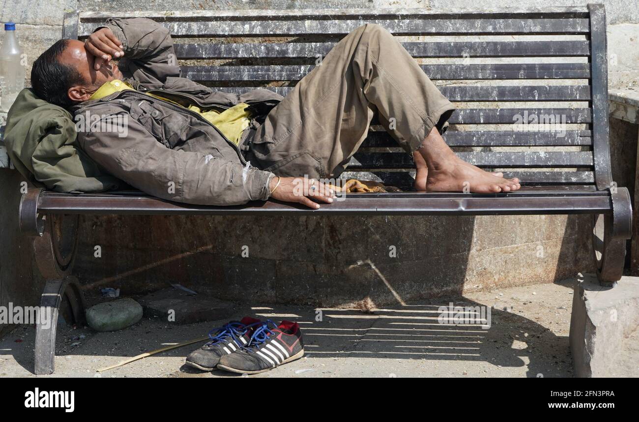 Poor homeless beggar man or refugee sleeping on a dirty wooden bench in ...
