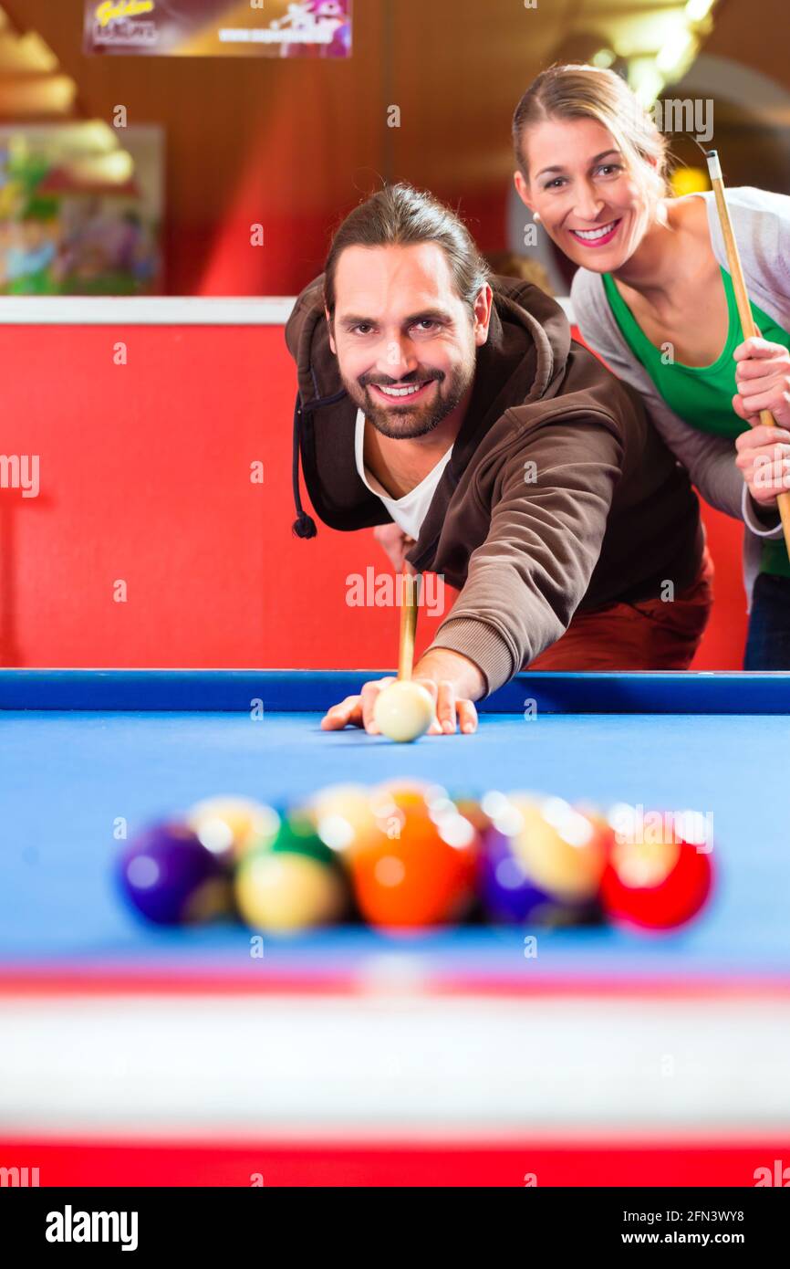 Couple or friends playing billiard with queue and balls on pool table ...