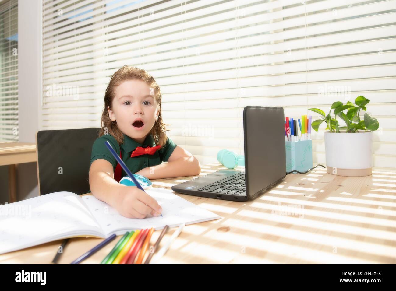 Excited pupil writing at notebook in classroom at the elementary school ...