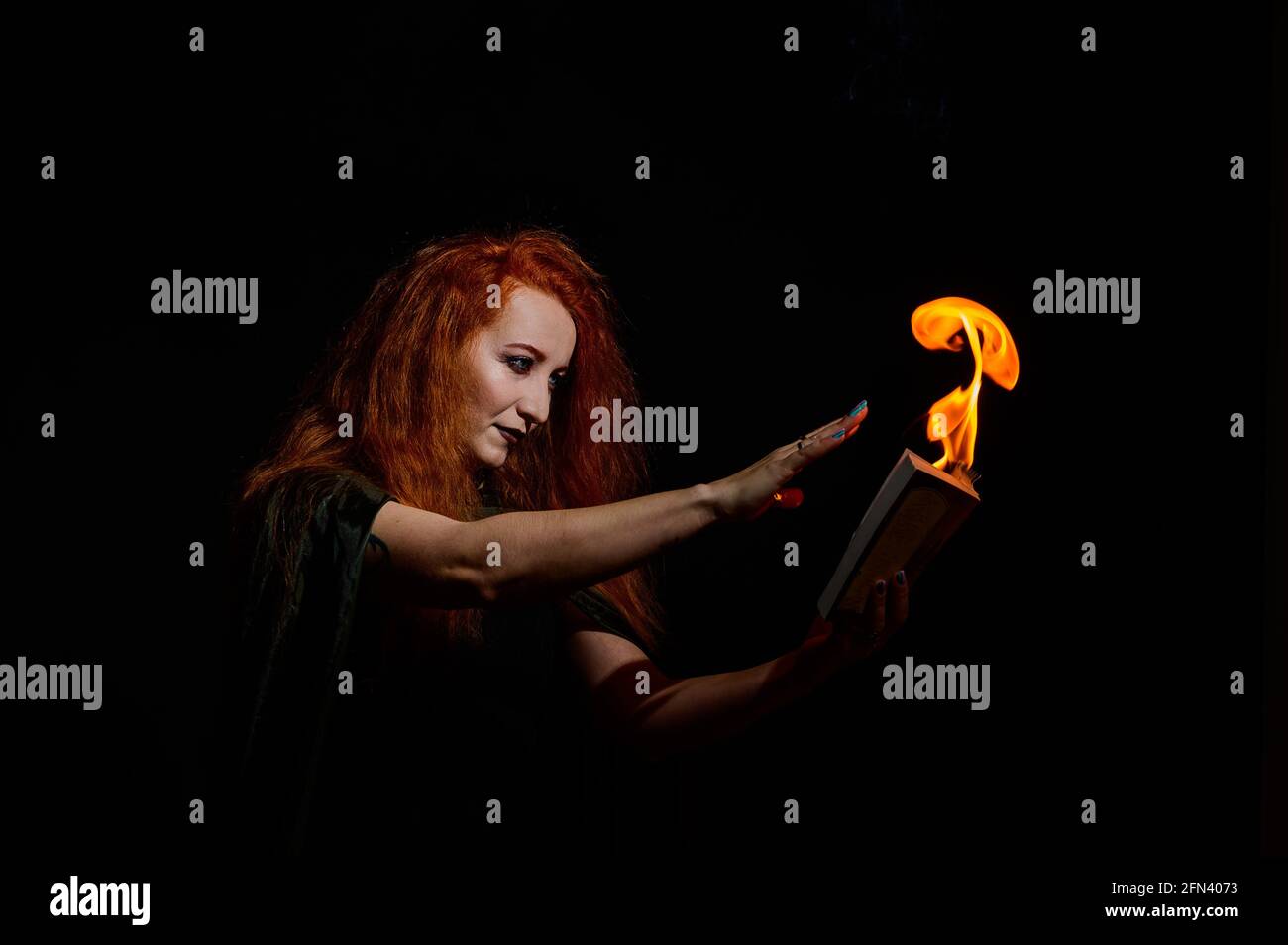 An ominous witch with long curly hair holds a magical fire. Tongues of ...