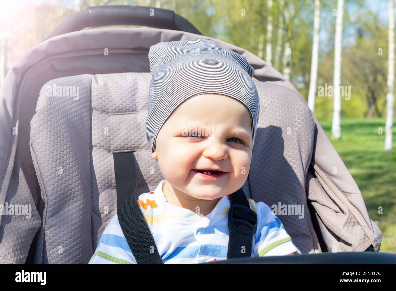 Adorable happy caucasian baby boy sitting in grey stroller in park ...