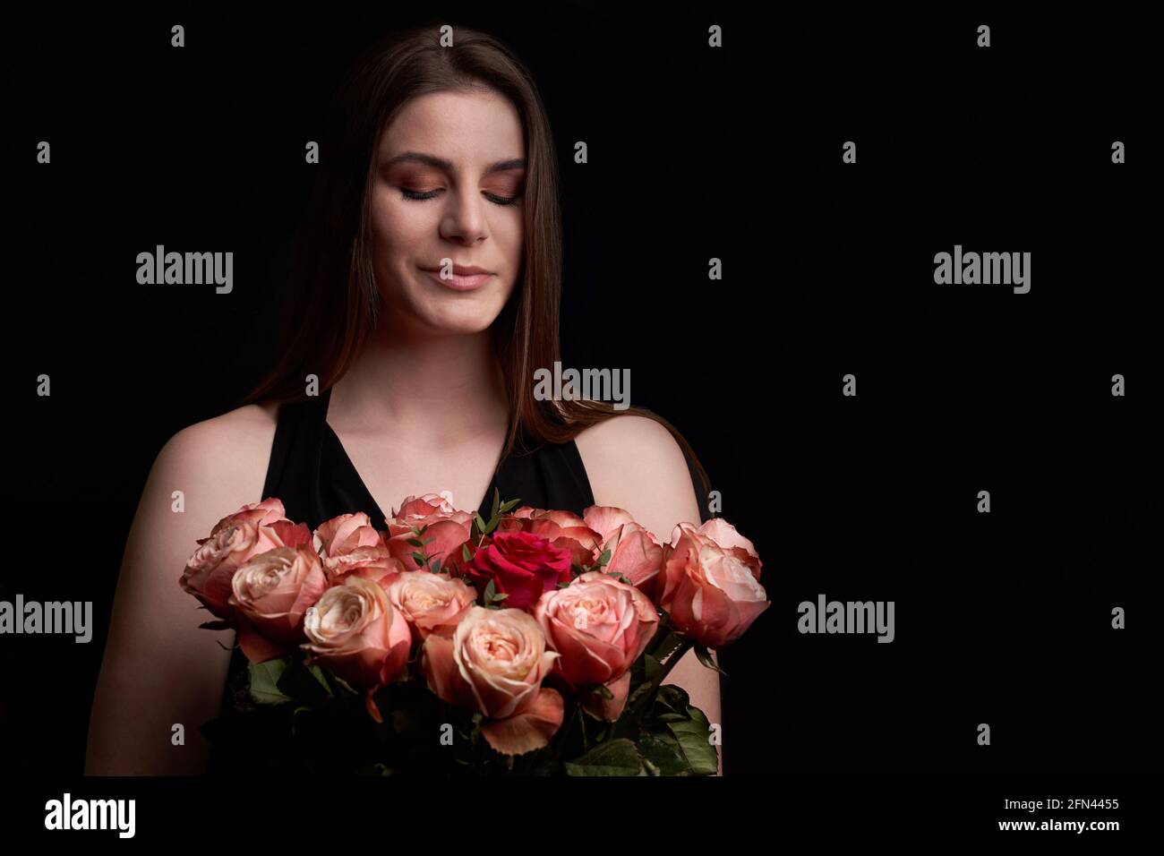 Teenage girl holding bunch of pink roses and smiling on black ...