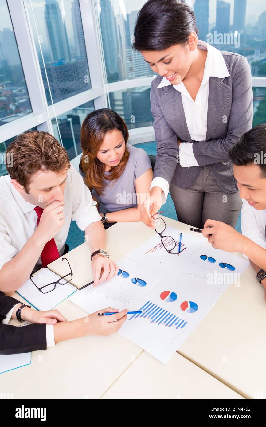 business team with Asian and Caucasian members discussing earnings with ...