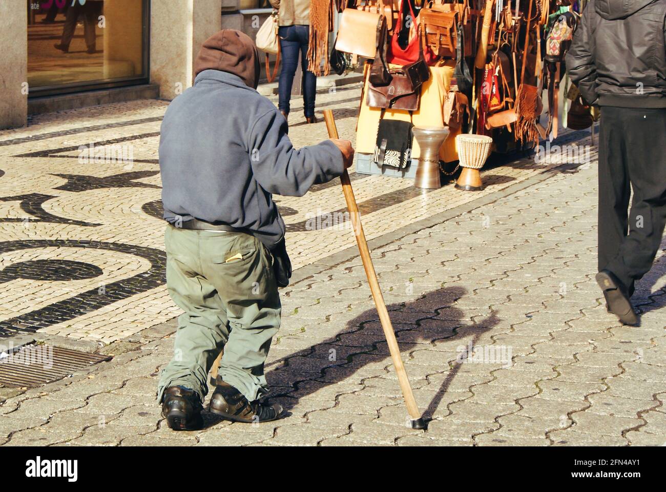 Old lame tramp walks holding a stick. Back view of a poor man trudging ...