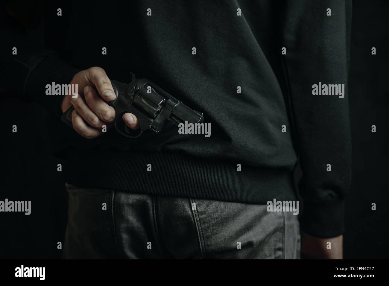 Man in grey cloth holds firearm behind his back. Revolver in men's hand ...