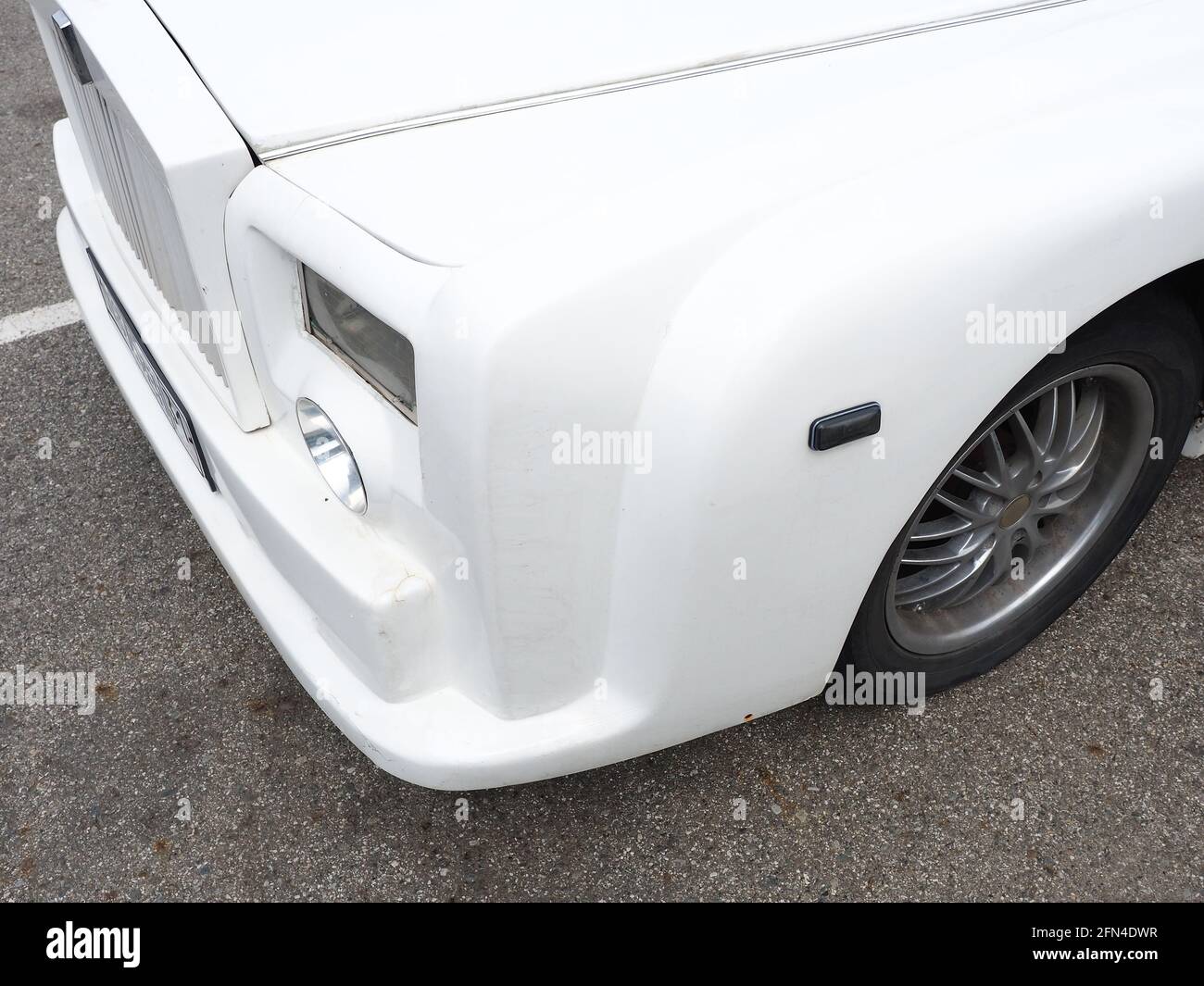 Fragment of a white matte car with square headlights and cracks on body ...