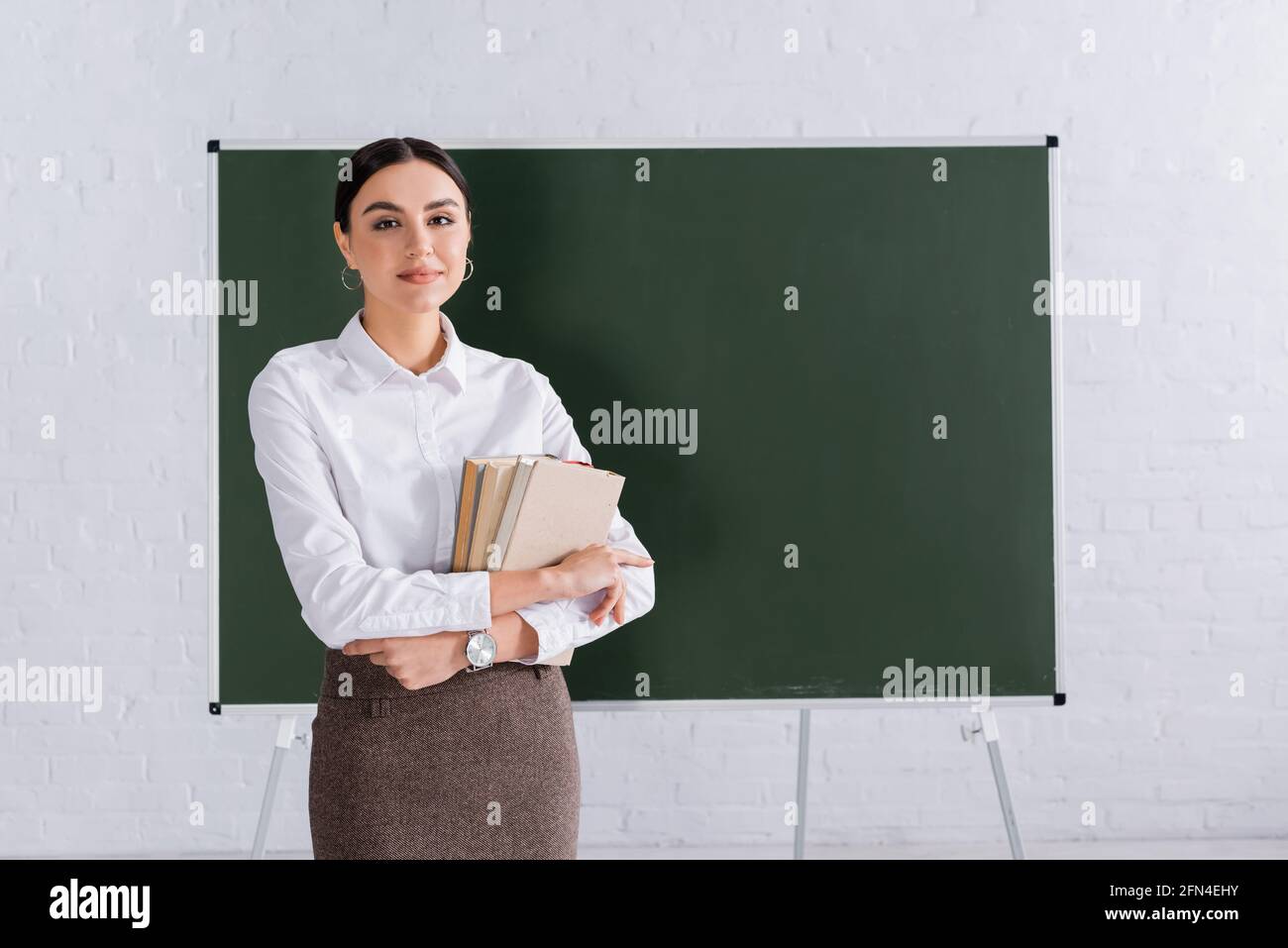 Young teacher with books standing near chalkboard in classroom Stock ...