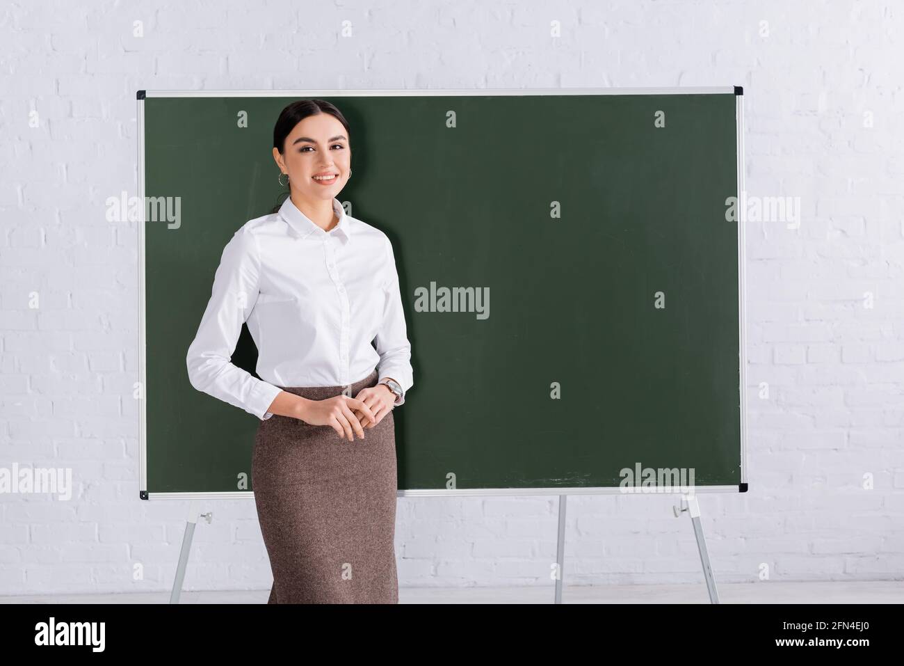 Positive teacher in formal wear standing near chalkboard with copy ...
