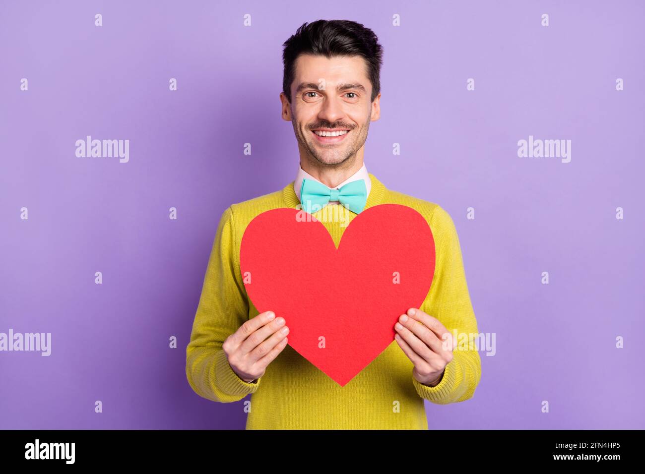Portrait of brunet optimistic guy hold paper heart wear yellow sweater ...