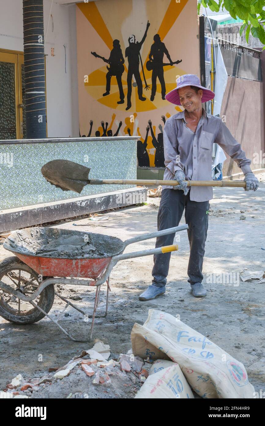 Vietnamese manual labourer shovelling cement into wheelbarrow, Da Nang ...