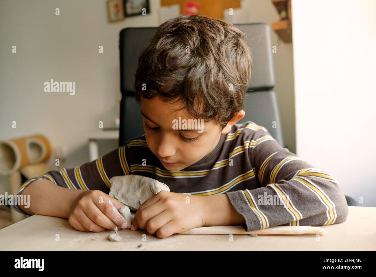 child playing with clay at home during quarantine. focused boy creating ...