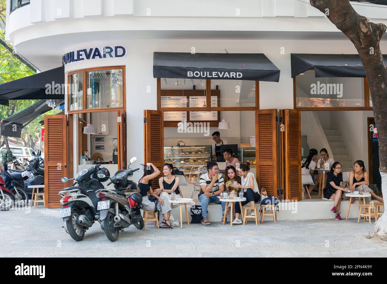 Vietnamese friends sit at pavement tables outside coffee shop, Da Nang ...