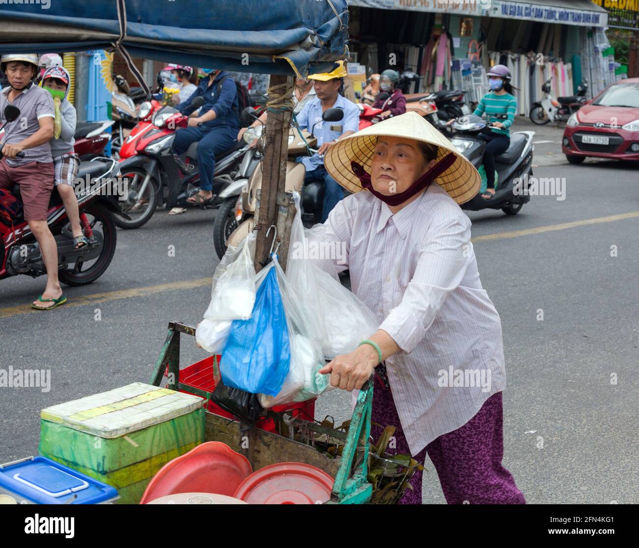 Elderly Vietnamese female pushes food cart through the busy streets of ...