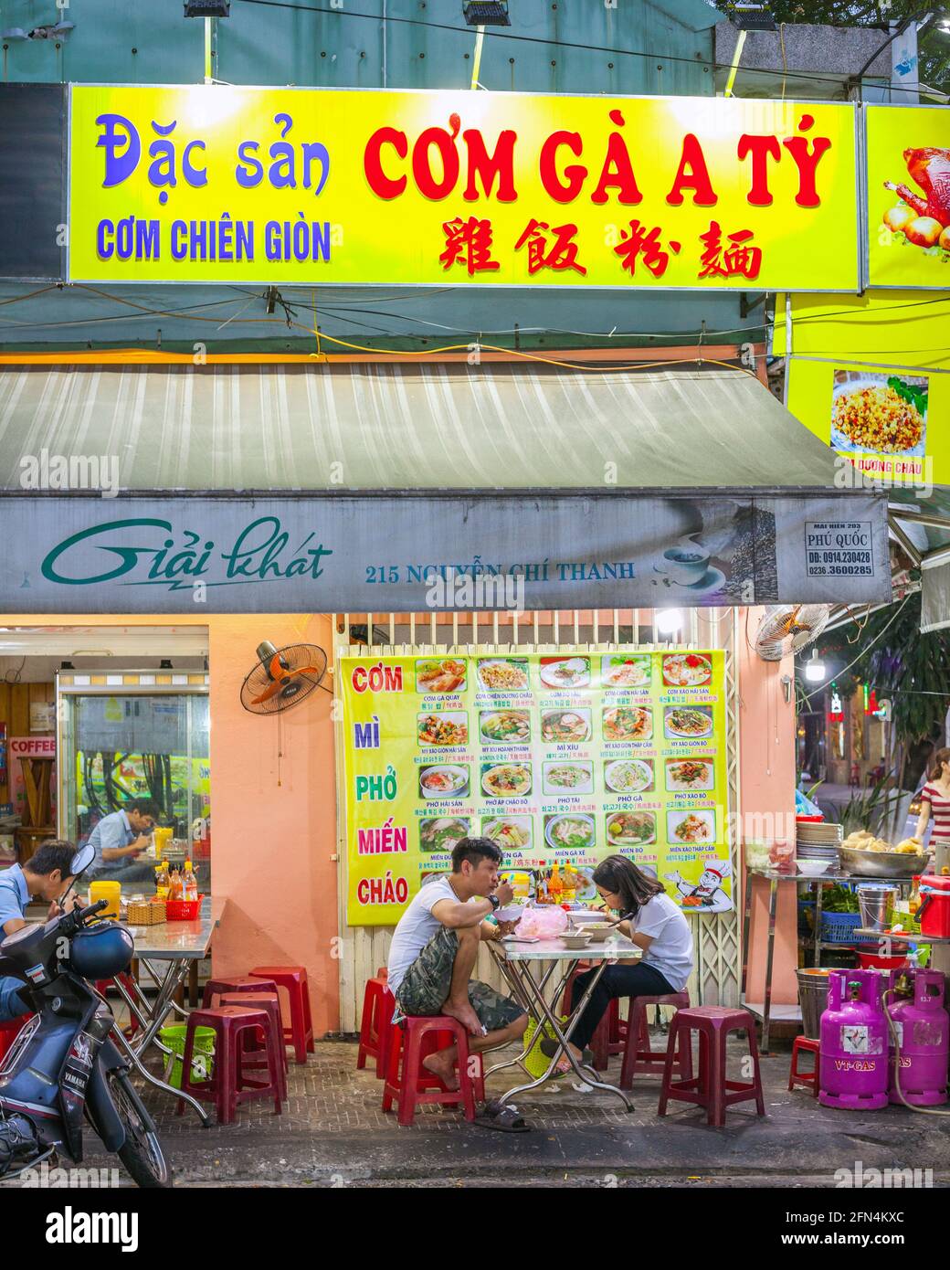 Vietnamese couple sit dining on pavement outside restaurant with garish ...