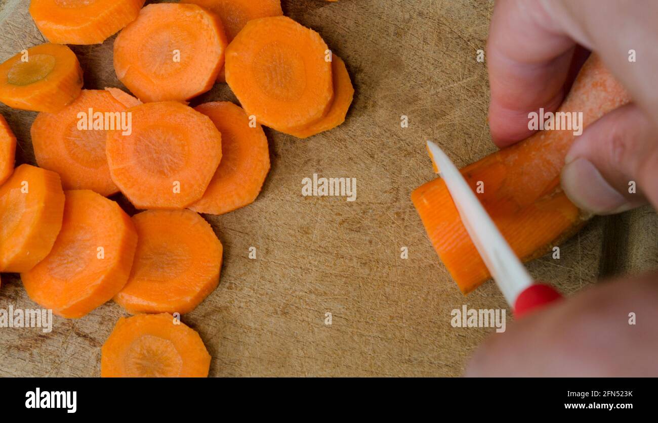 cutting carrots, top view with ceramic knife on wooden plate, natural ...
