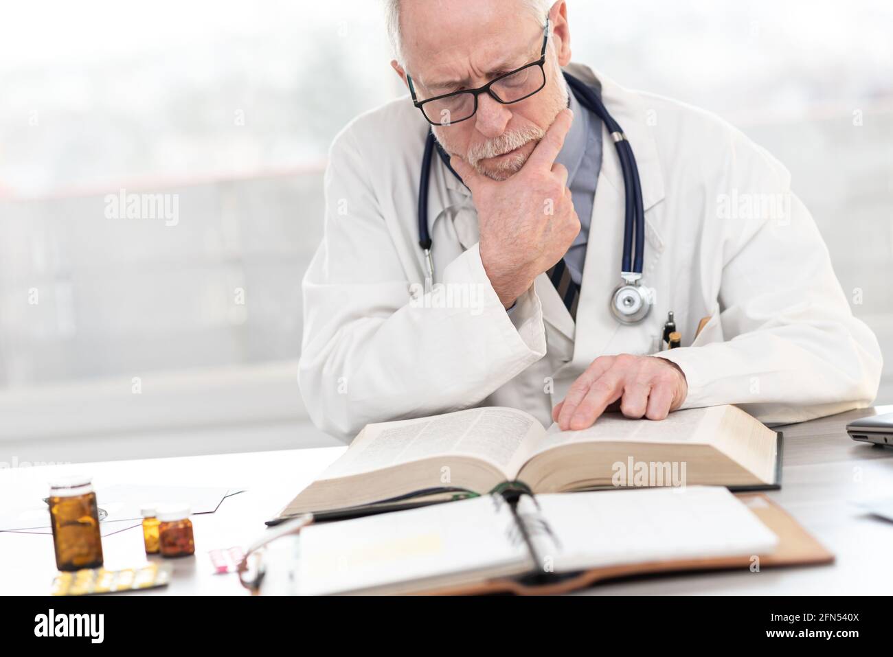 Senior doctor reading a textbook in medical office Stock Photo - Alamy