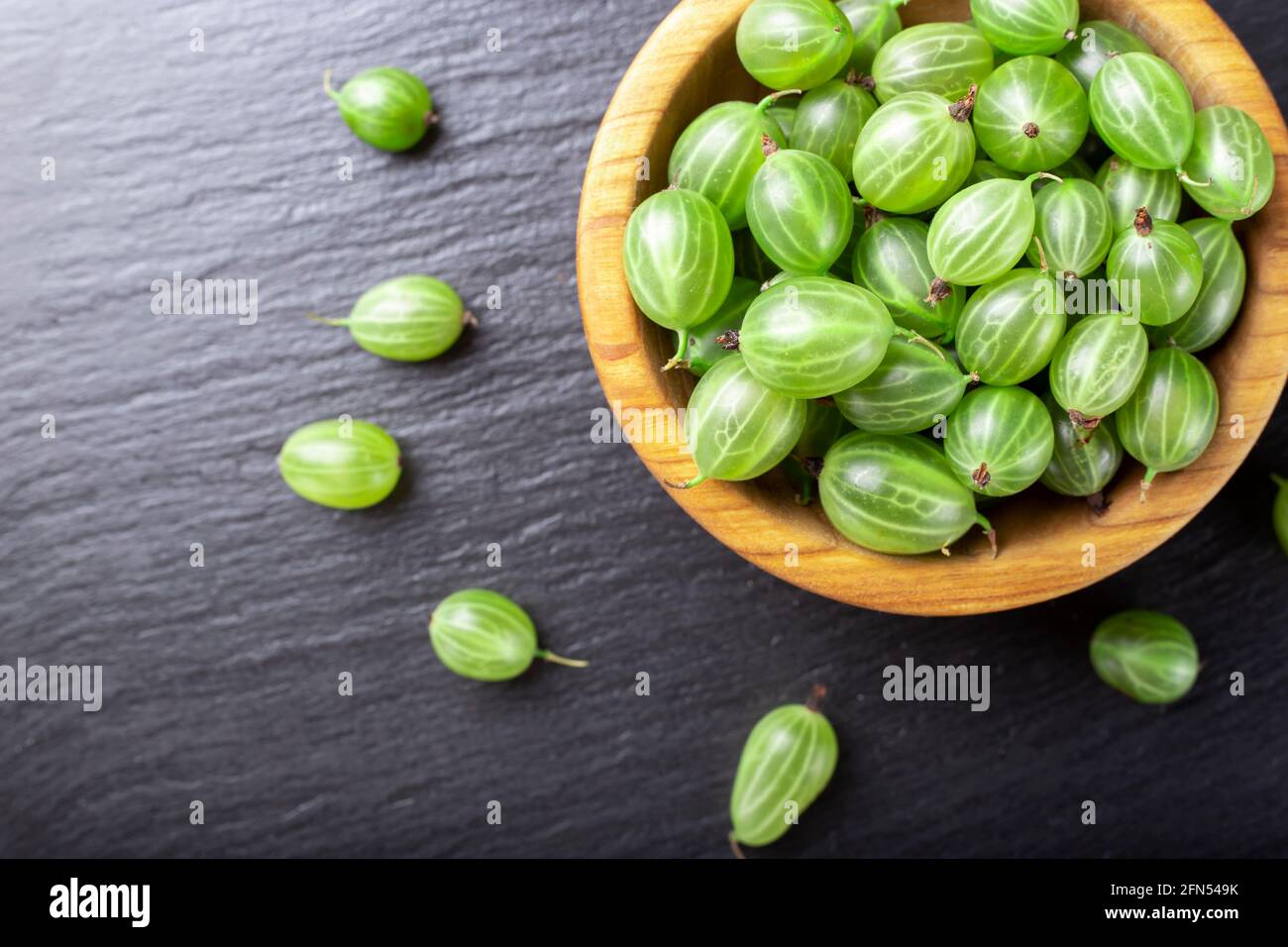 Fresh gooseberries in wooden bowl on black stone slate background. Top ...