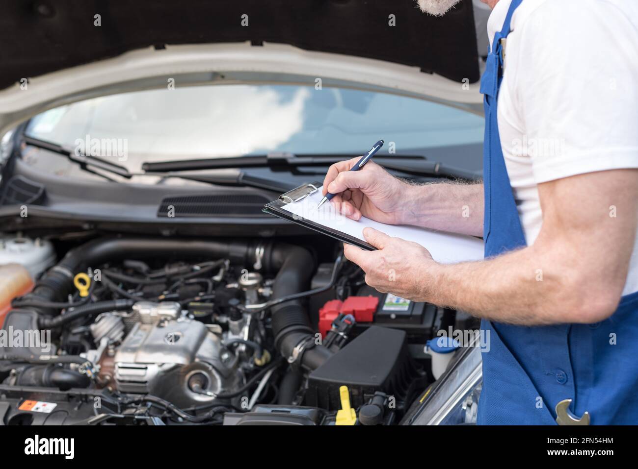 Car mechanic checking a car engine and writing on clipboard Stock Photo ...