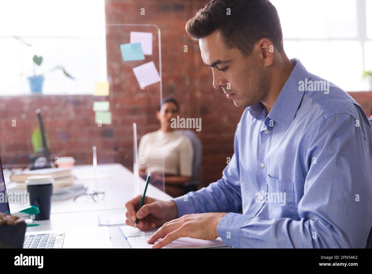 Caucasian man taking notes while sitting on his desk at modern office ...