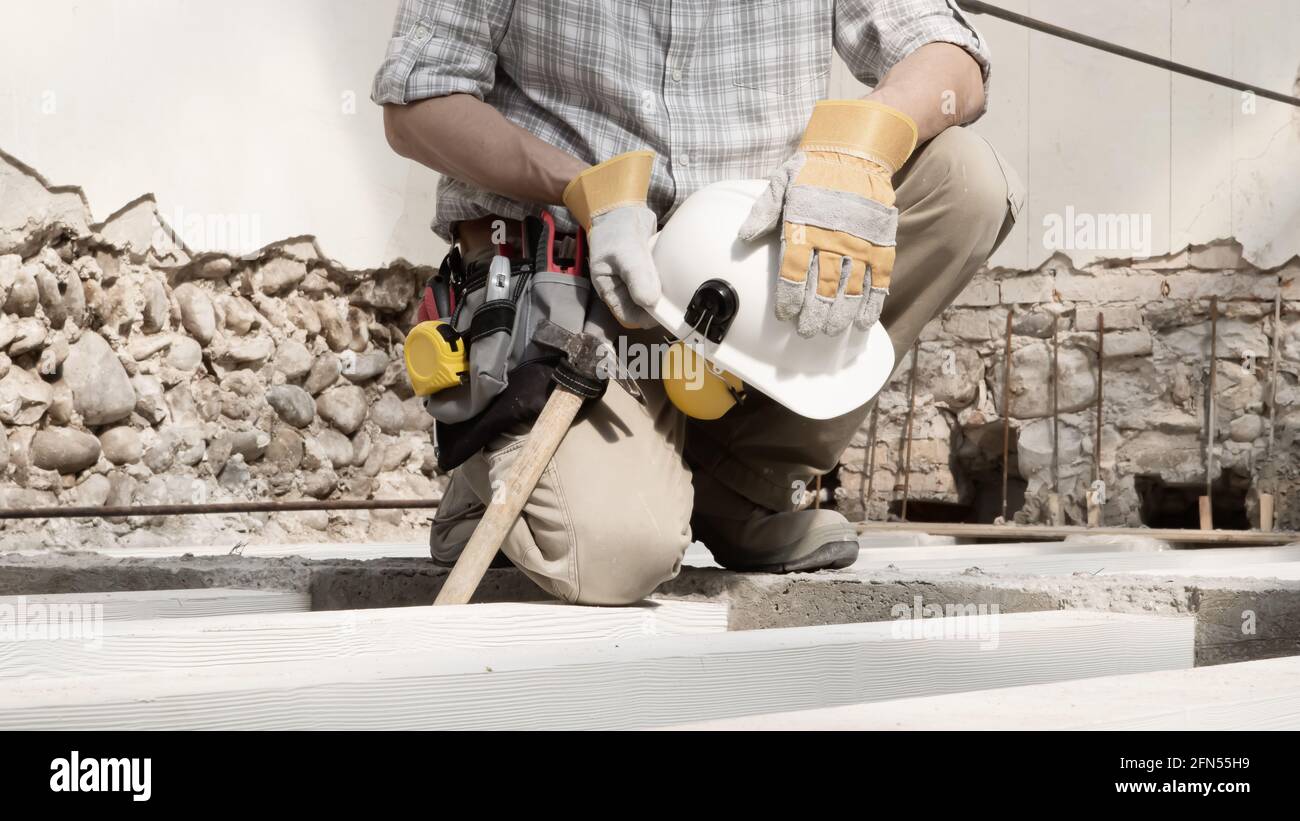 construction worker with tool bag wears gloves and holds helmet in ...