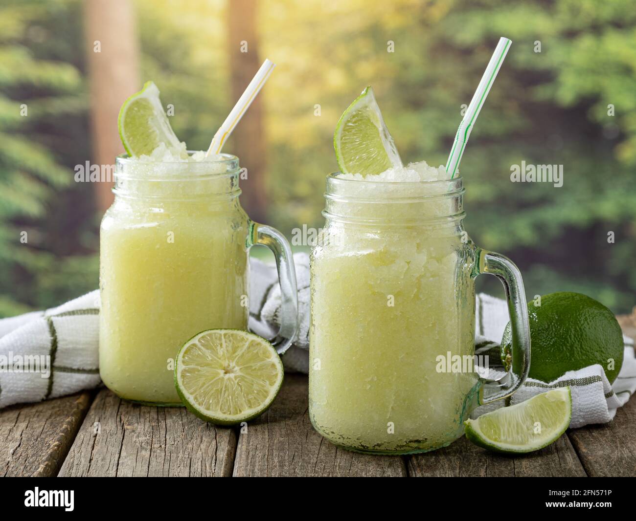 Slush drink with lime in glass jars outside on a wooden table with ...