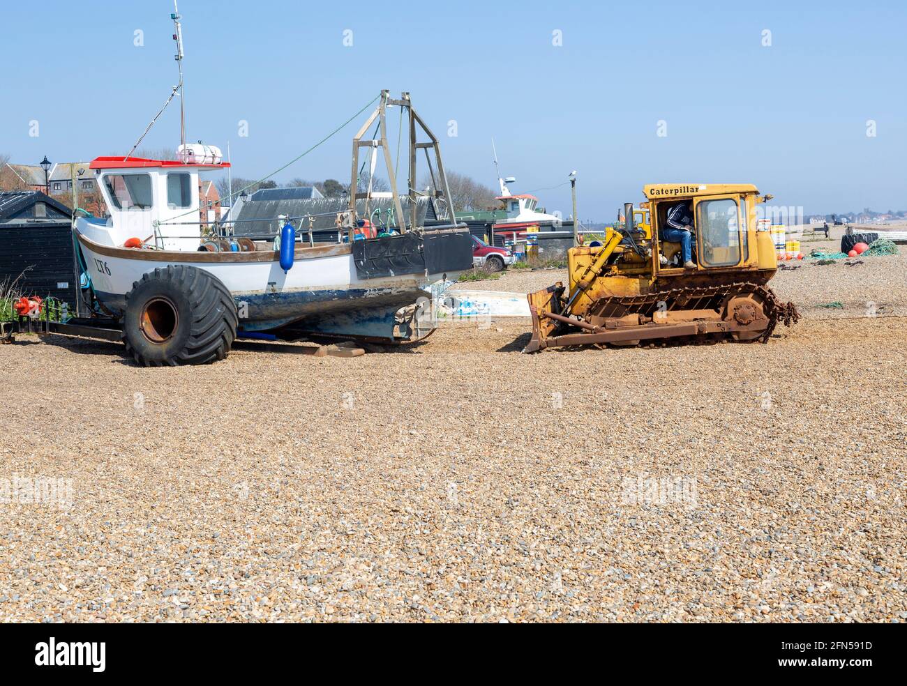 Caterpillar bulldozer machine and fishing boats on shingle beach ...