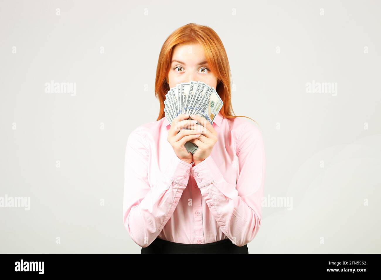 Young beautiful redhead woman covering her face with fistful of money ...