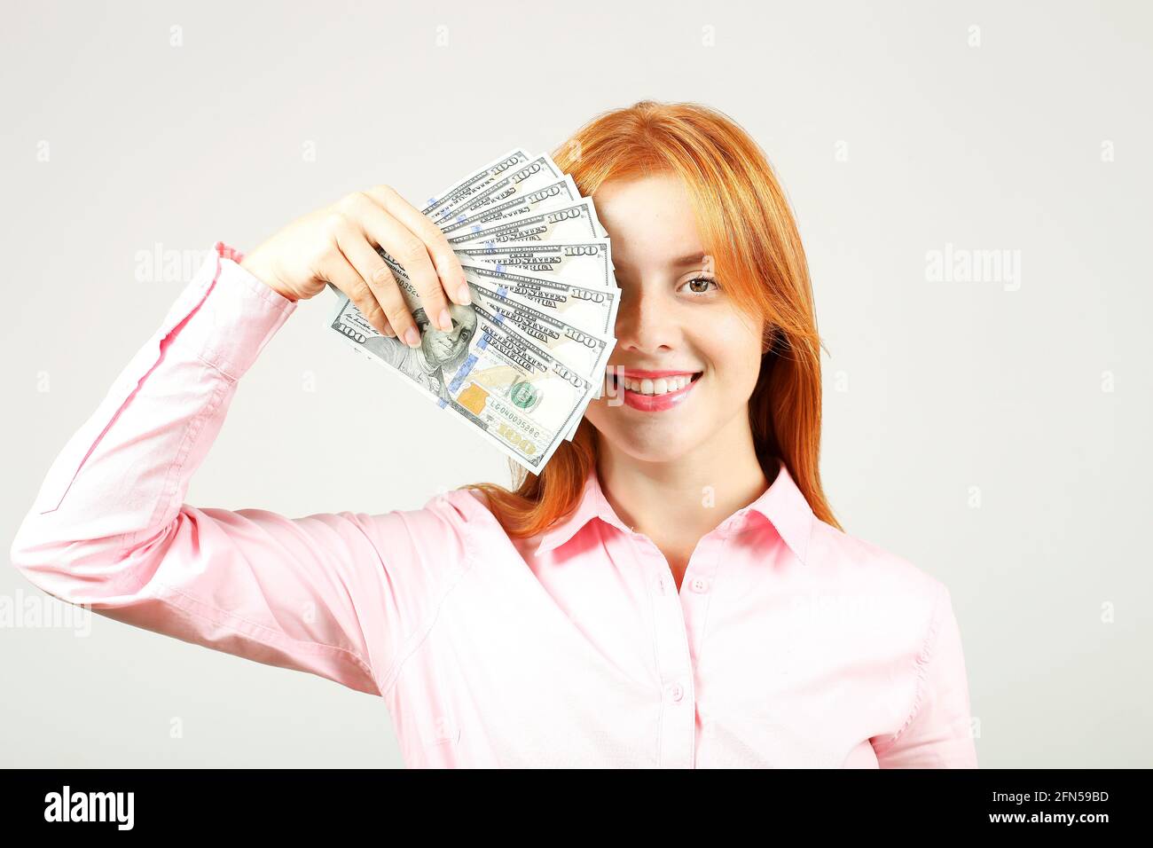 Young beautiful redhead woman covering her face with fistful of money ...