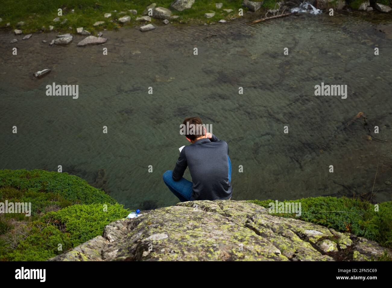 A teenager reading a book above a mountain stream in the French ...
