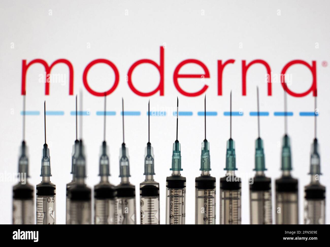 Medical syringes are pictured in front of the Moderna logo in this ...