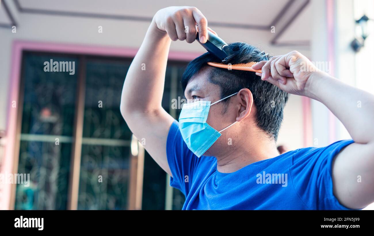 Man wear face mask and cutting hair personally himself with machine ...