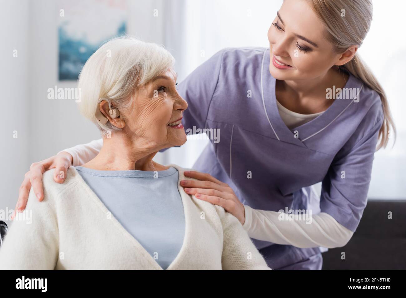 smiling social worker hugging shoulder of senior woman with hearing aid ...
