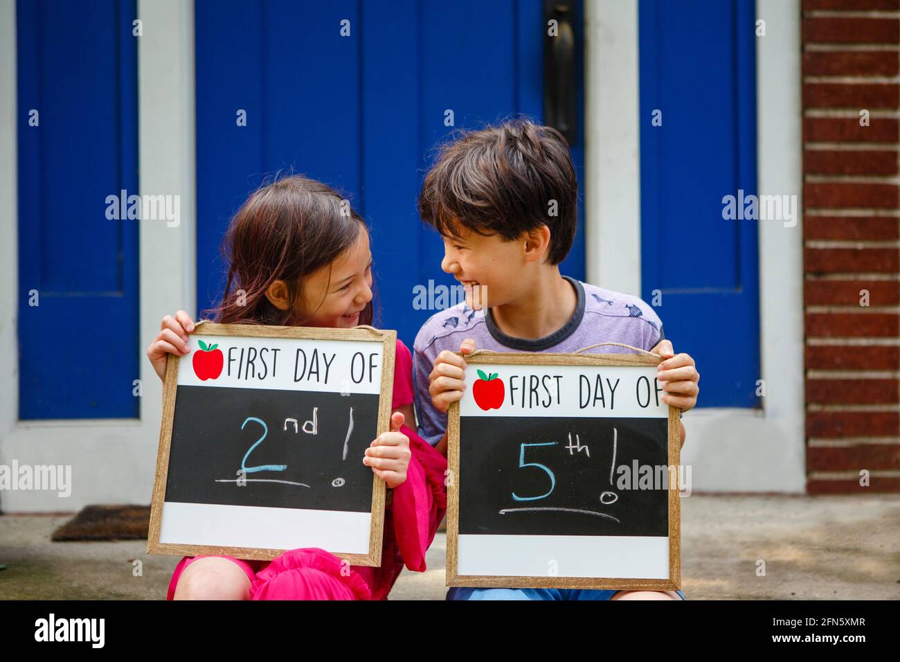 Two happy children sit together on stoop holding Back-to-School signs ...