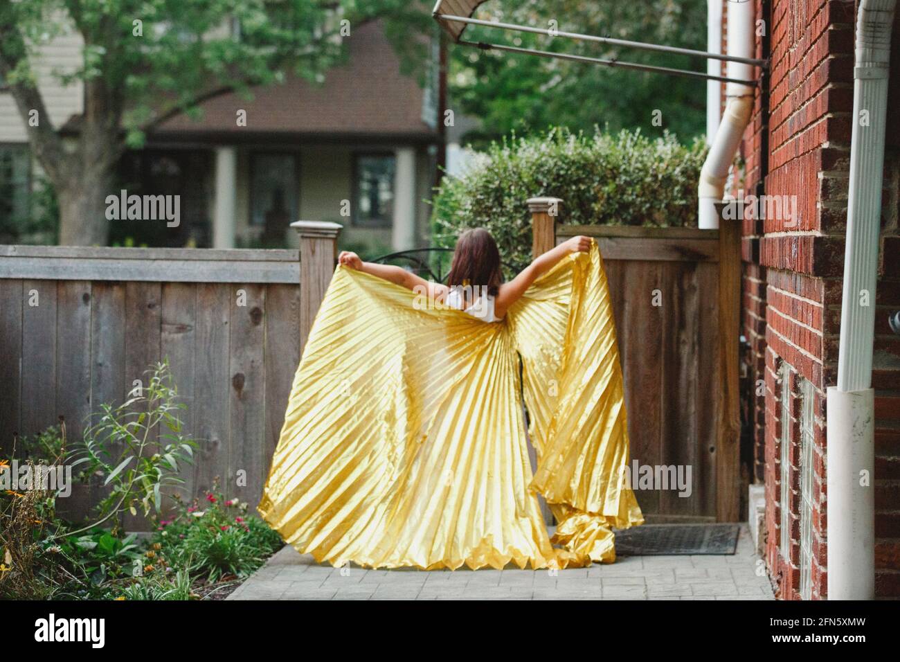 Rear-view of child in long golden cape with arms outstretched outside ...