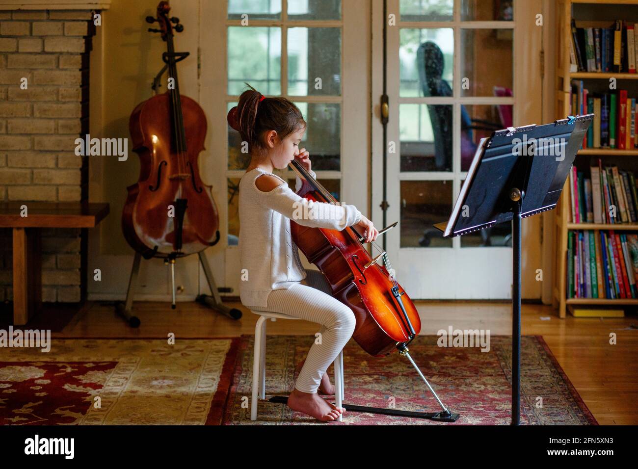 a focused graceful child practices cello in window light at home Stock ...
