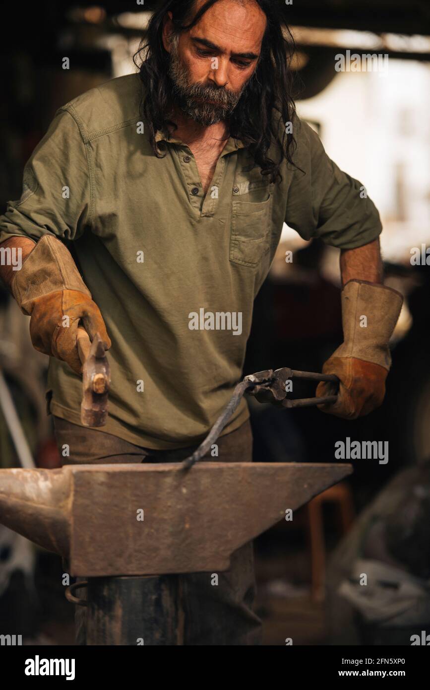 Blacksmith working a piece of steel with a sledgehammer on an anvil ...