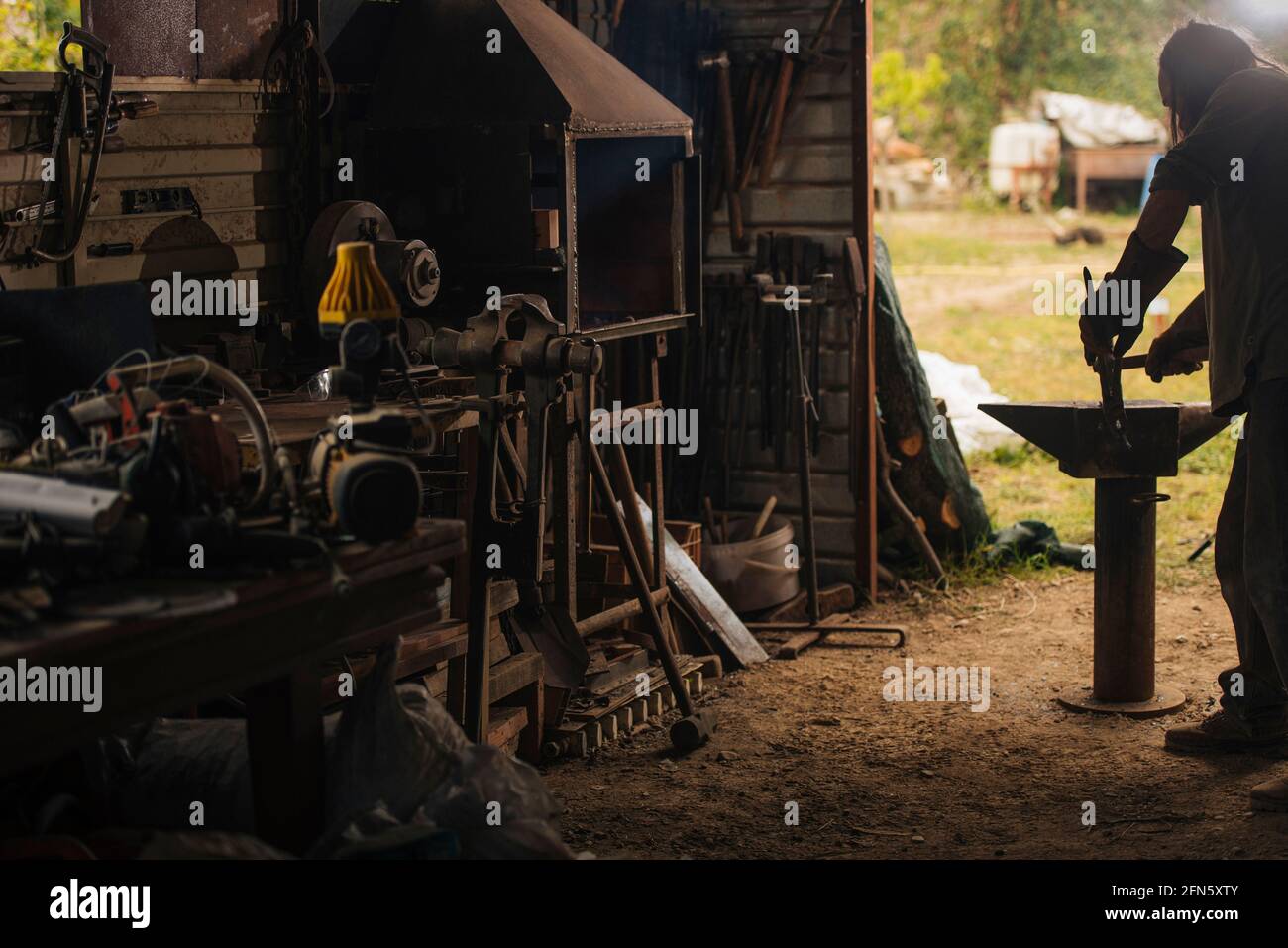 Blacksmith working a piece of steel with a sledgehammer on an anvil ...