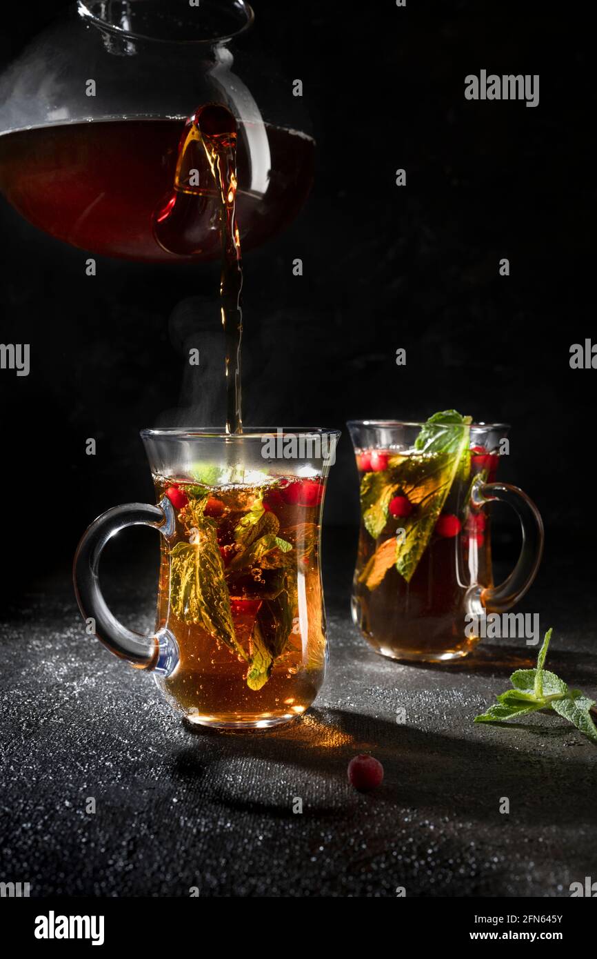 Pour black tea from a transparent teapot into a cup on black backround ...