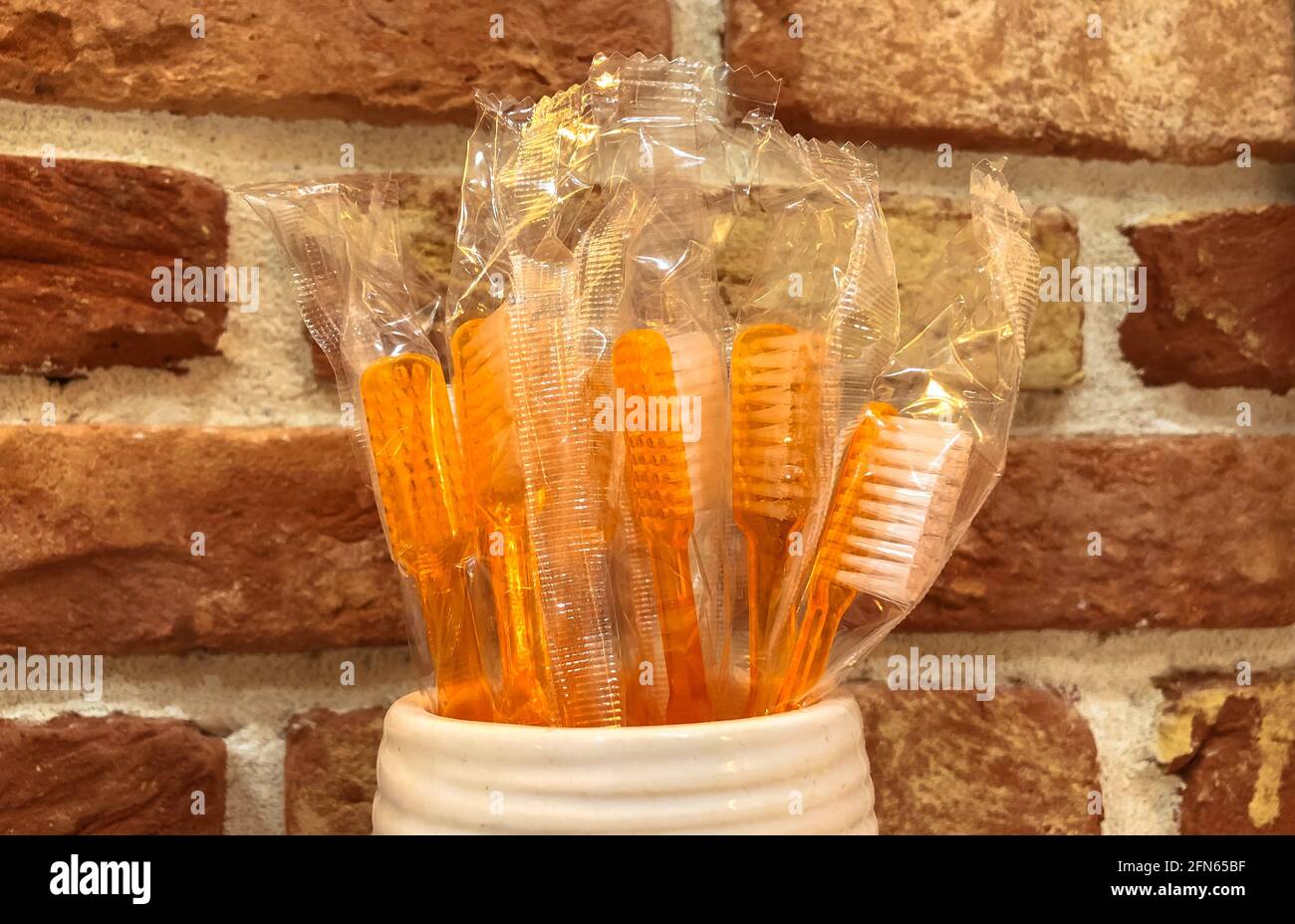 Disposable plastic orange toothbrushes in a ceramic cup against a red ...