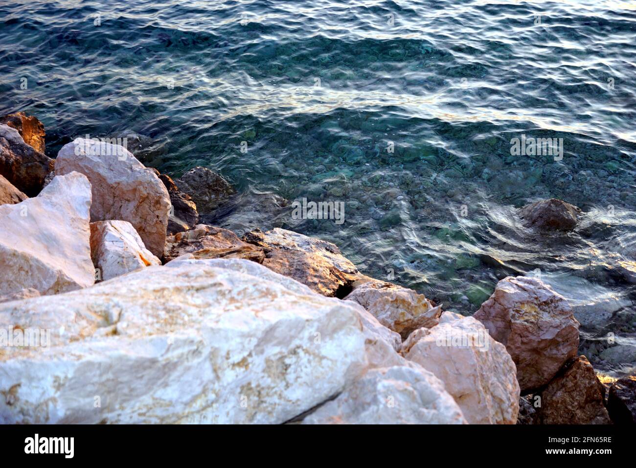 Wavy blue sea water surface with big white stone rocks in the ...