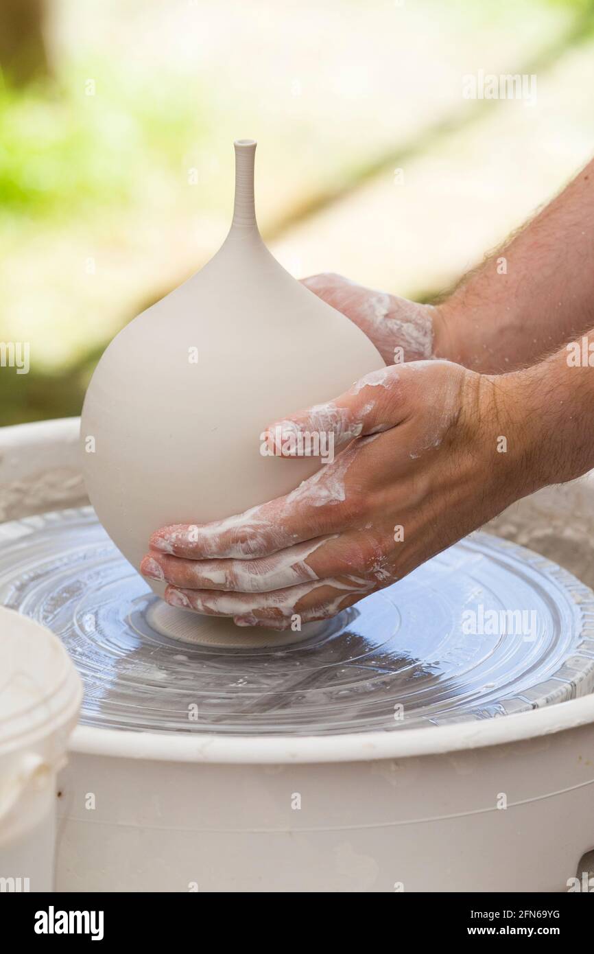 Potters hands skilfully hand throwing a ceramic thrown clay vase pot on ...