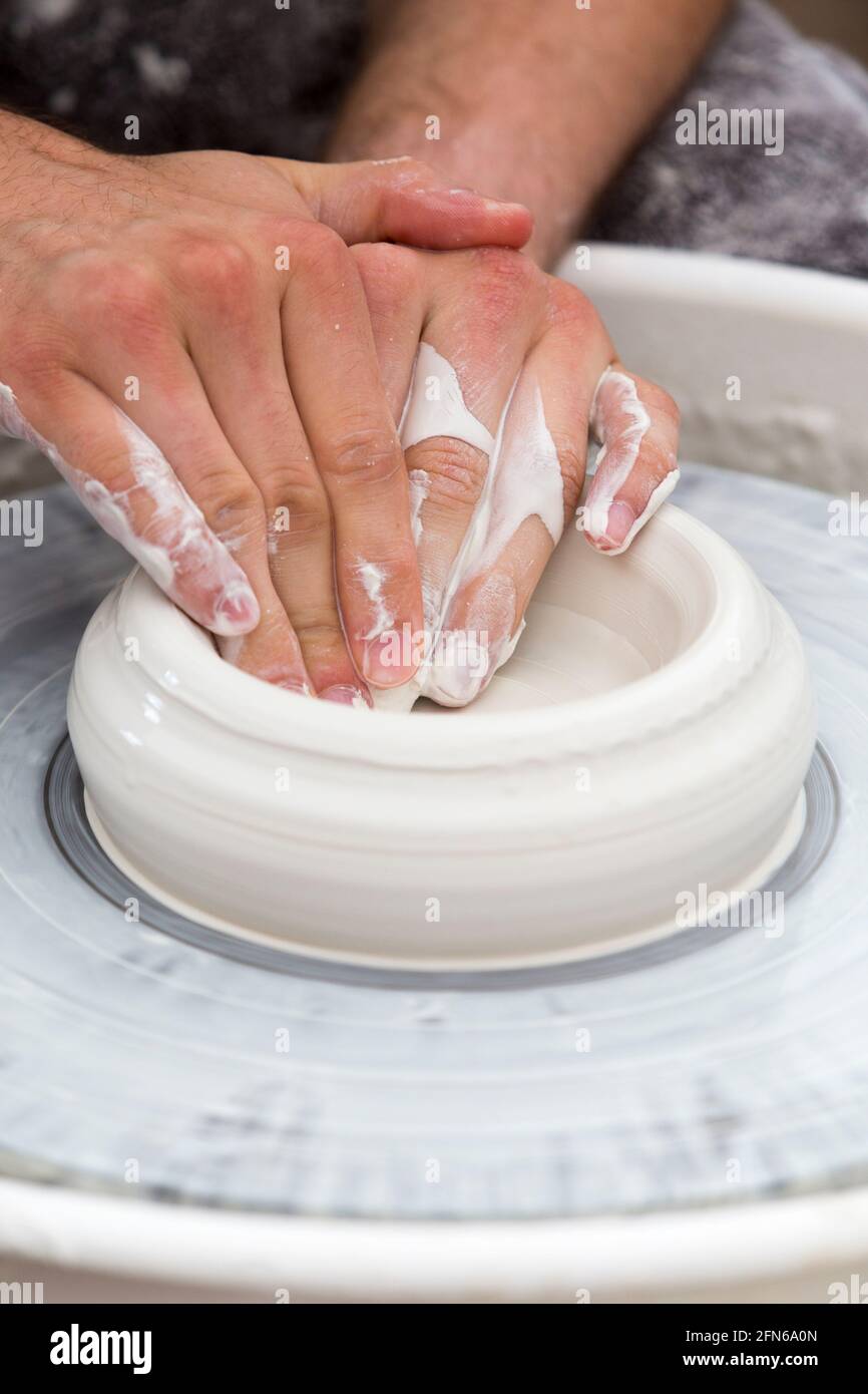 Potters hands skilfully hand throwing a ceramic thrown clay vase pot on ...