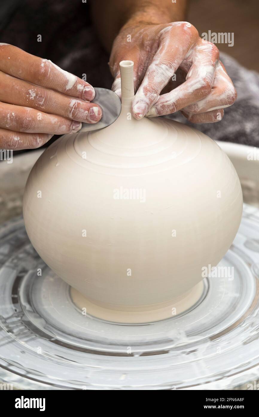 Potter / potters hands using a metal turning tool skilfully hand ...