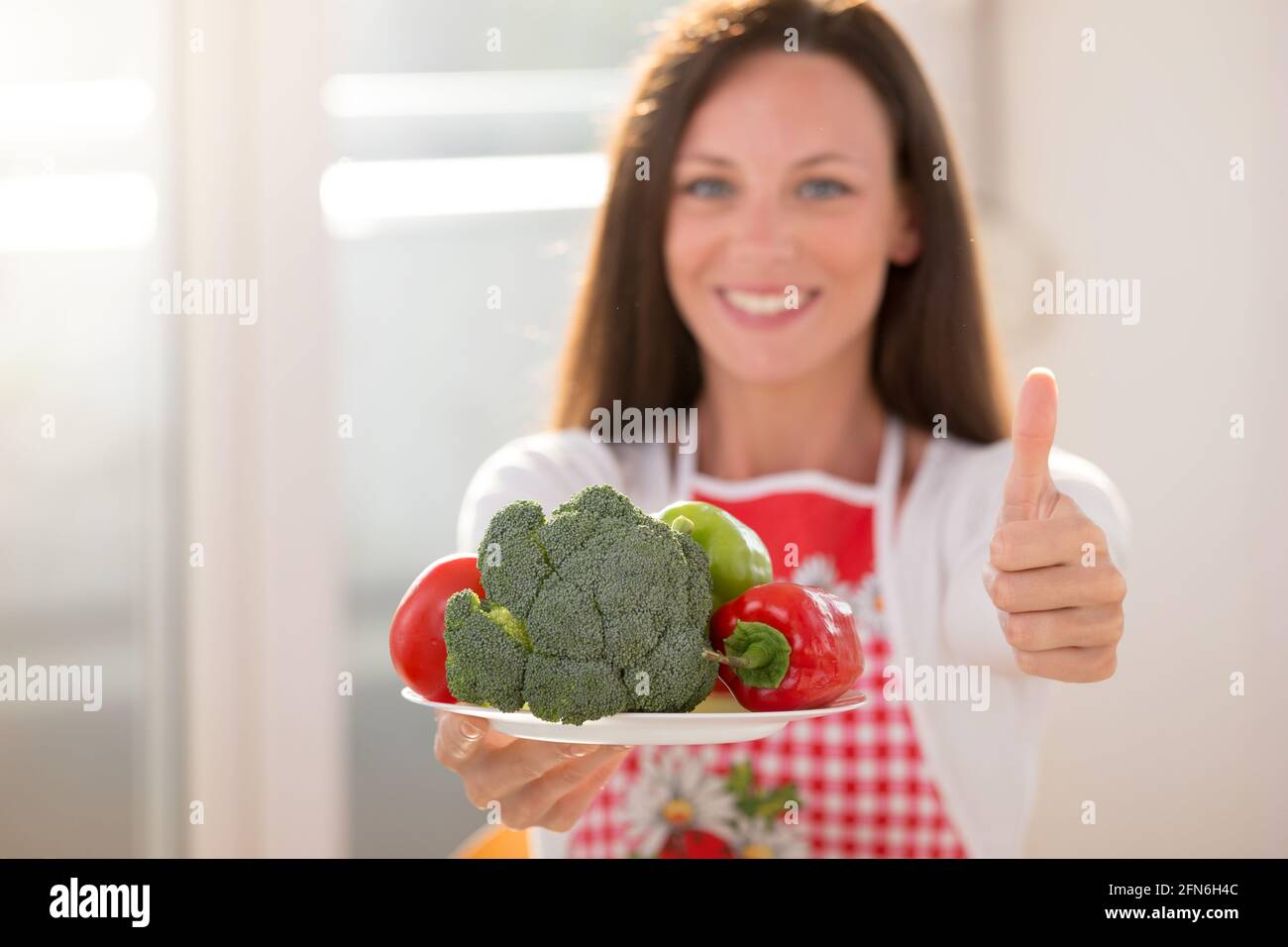 Pretty yoing girl holding plate with vegetables in one hand and showing ...