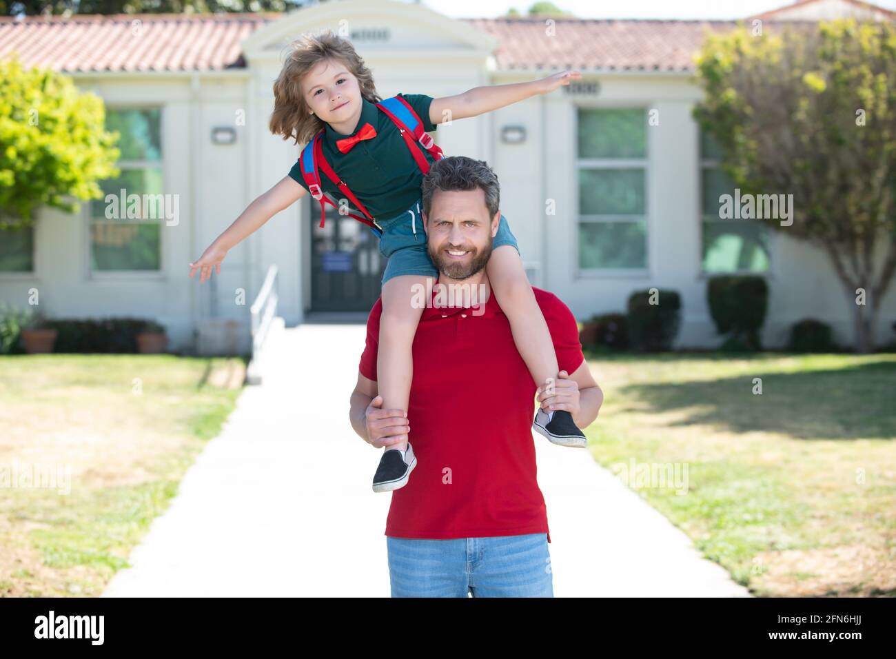 Father and son walking trough school park. Father giving son piggyback ...