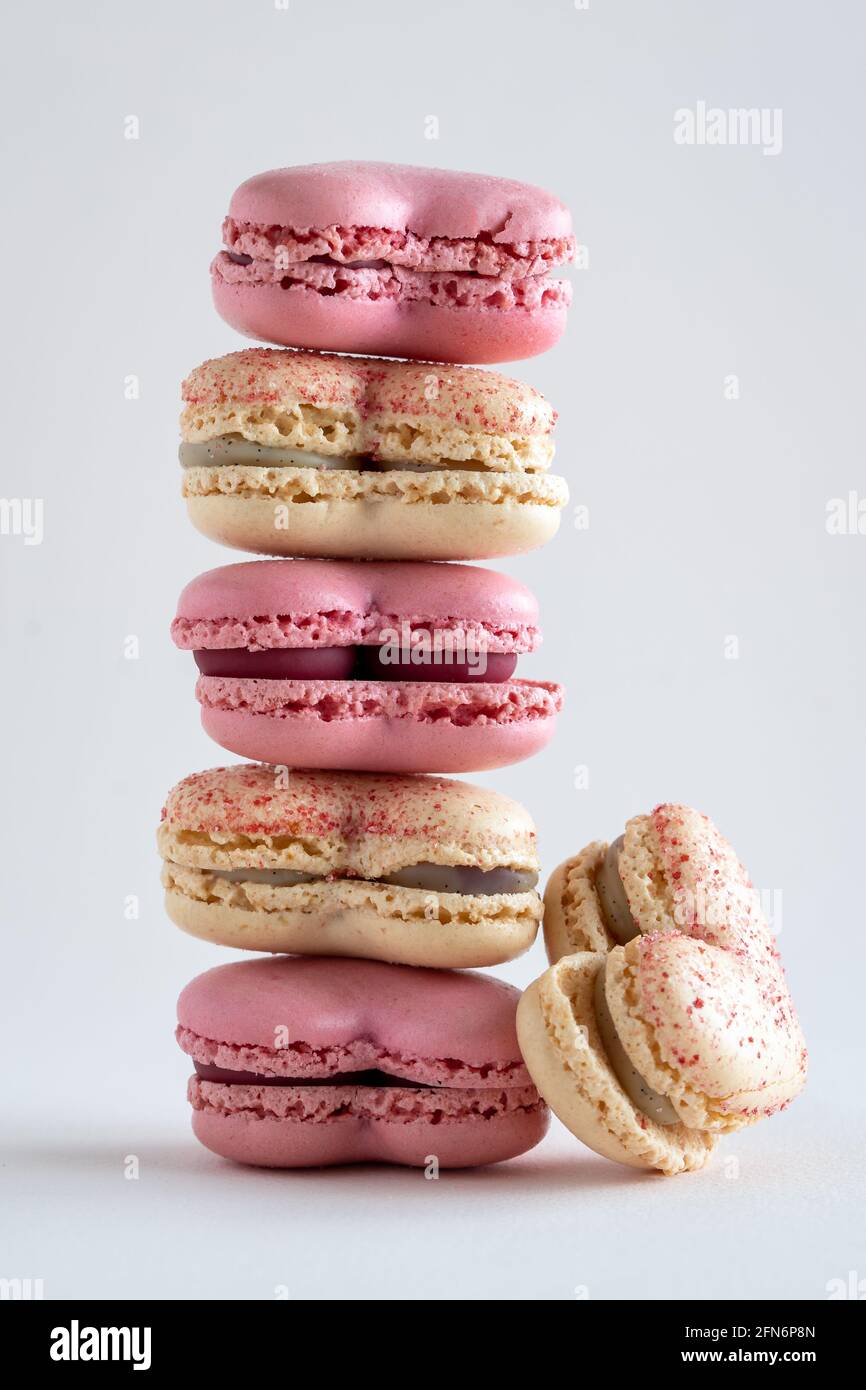 A large stack of French macarons in pink and yellow with one macaron on ...