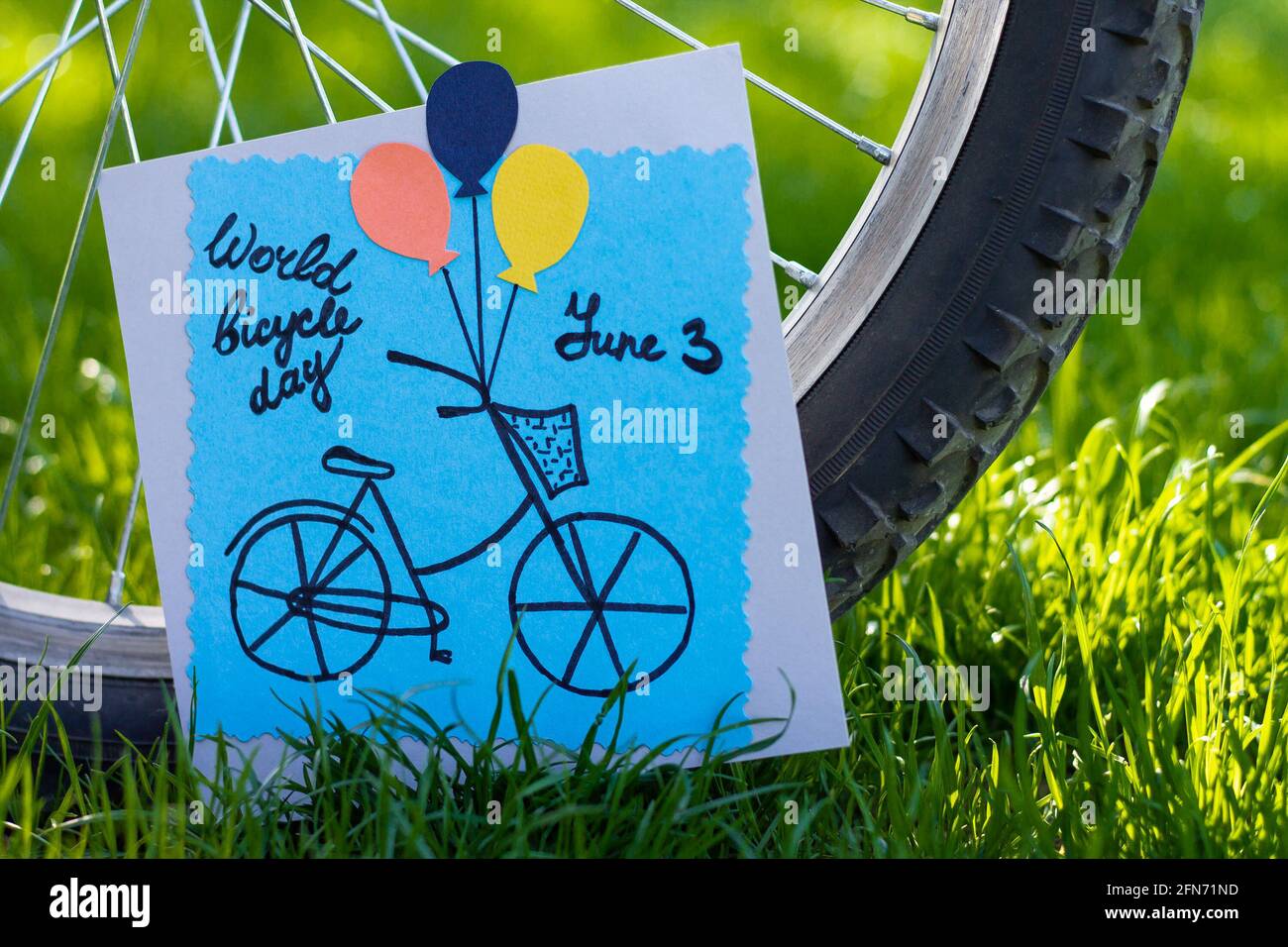 Handmade colored paper greeting card next to a bicycle wheel on grass ...
