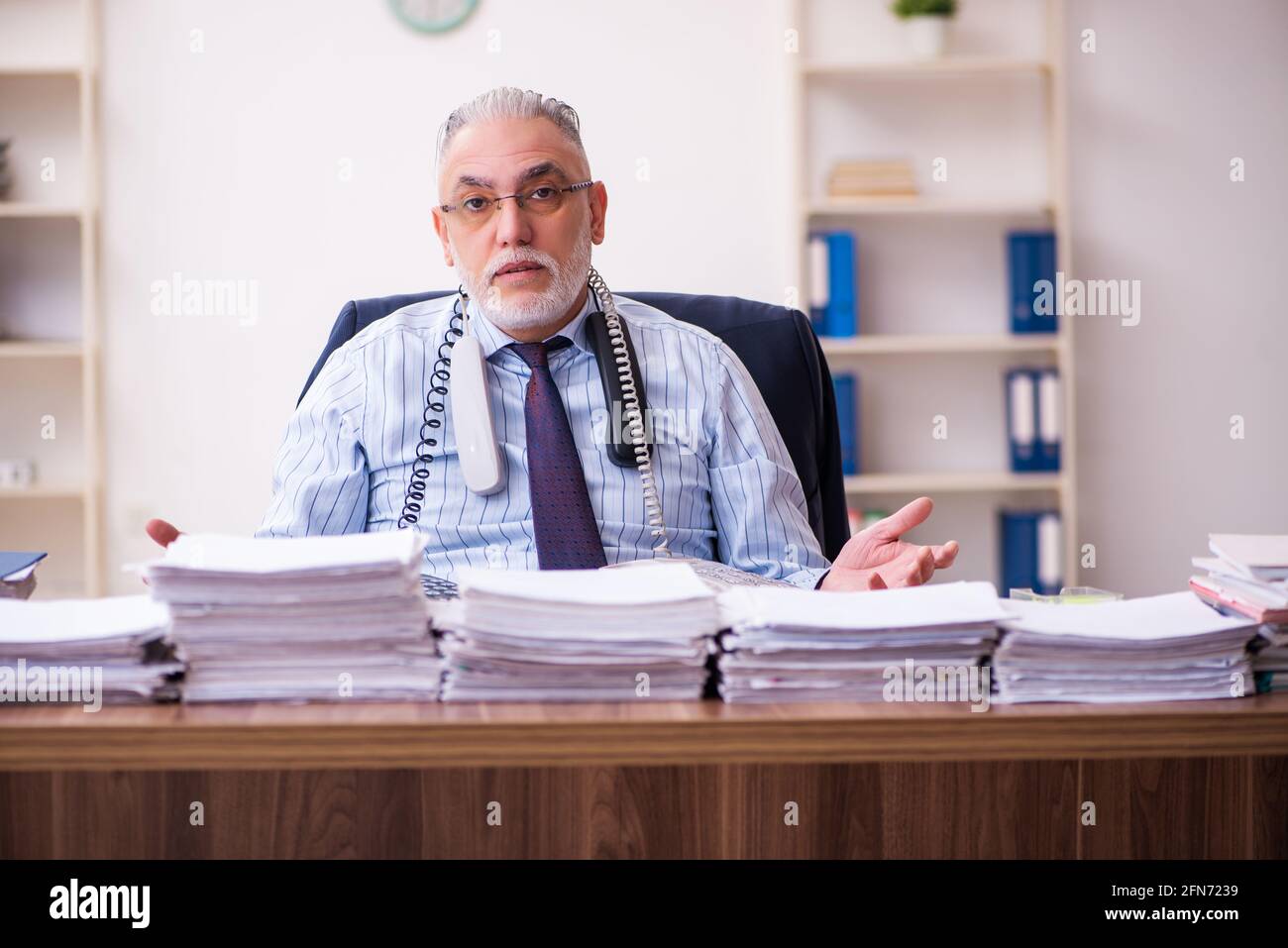 Old male employee unhappy with excessive work at workplace Stock Photo ...