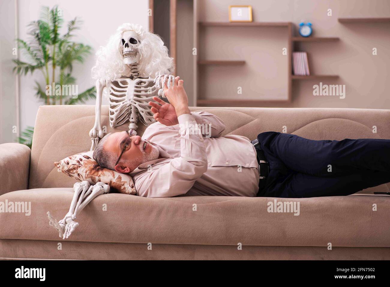 Old man sitting on the sofa with the female skeleton in undying love ...